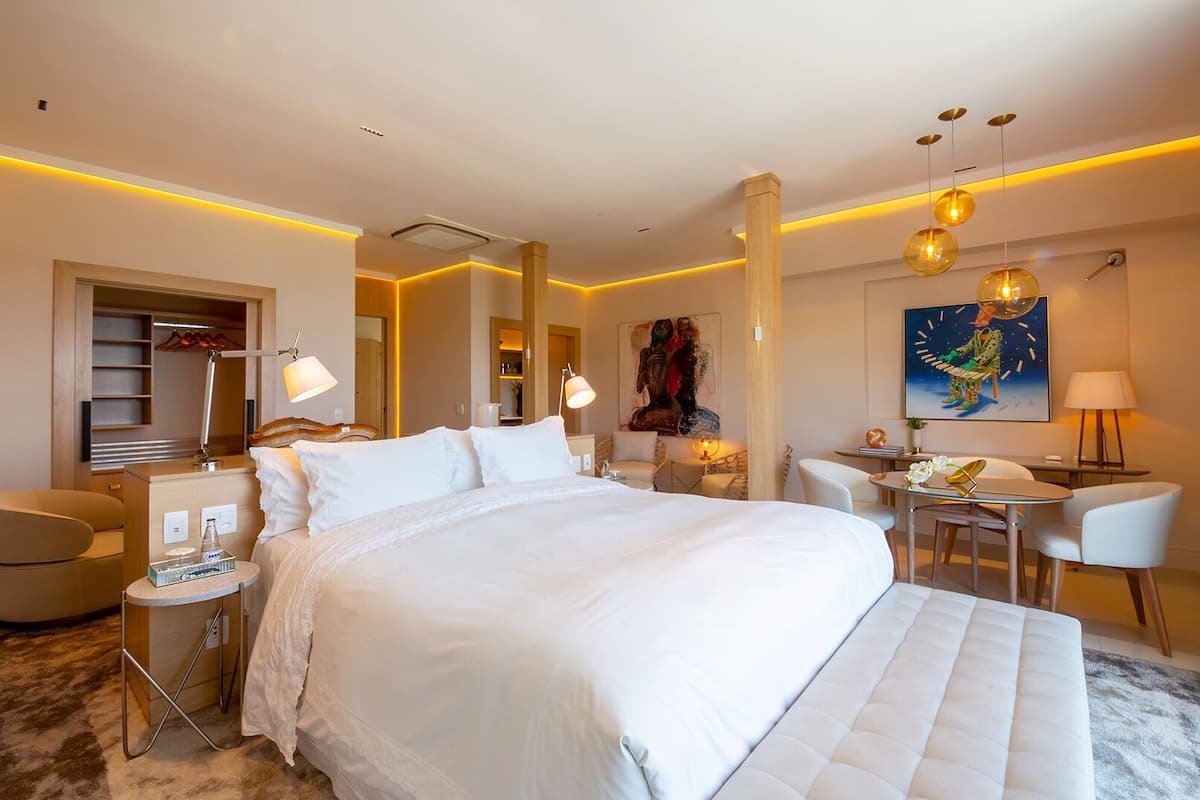 Quarto de hotel moderno com uma cama grande, mesas de cabeceira, uma escrivaninha e uma cadeira.