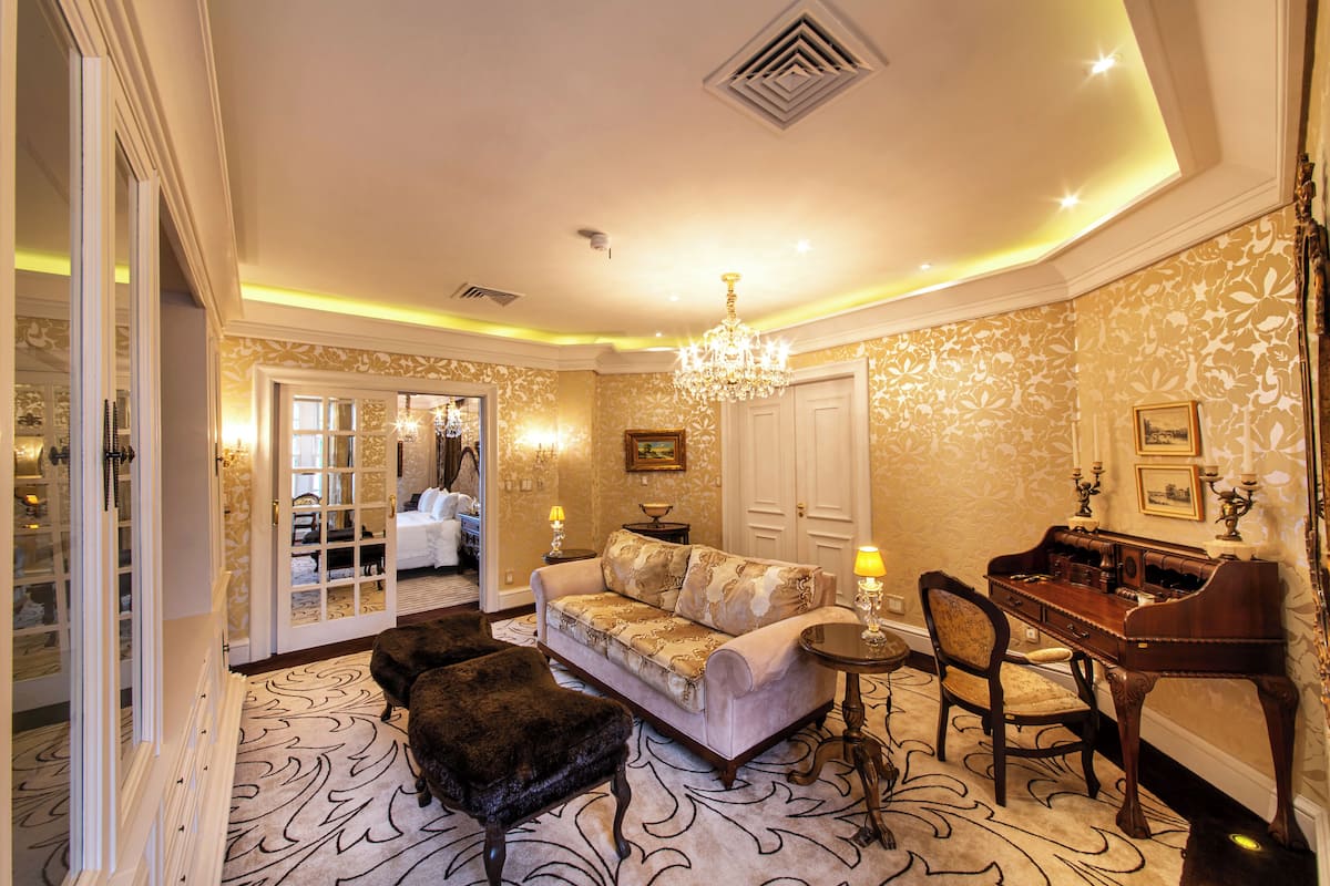 Um quarto com sofá, piano, lustre e tapete estampado.