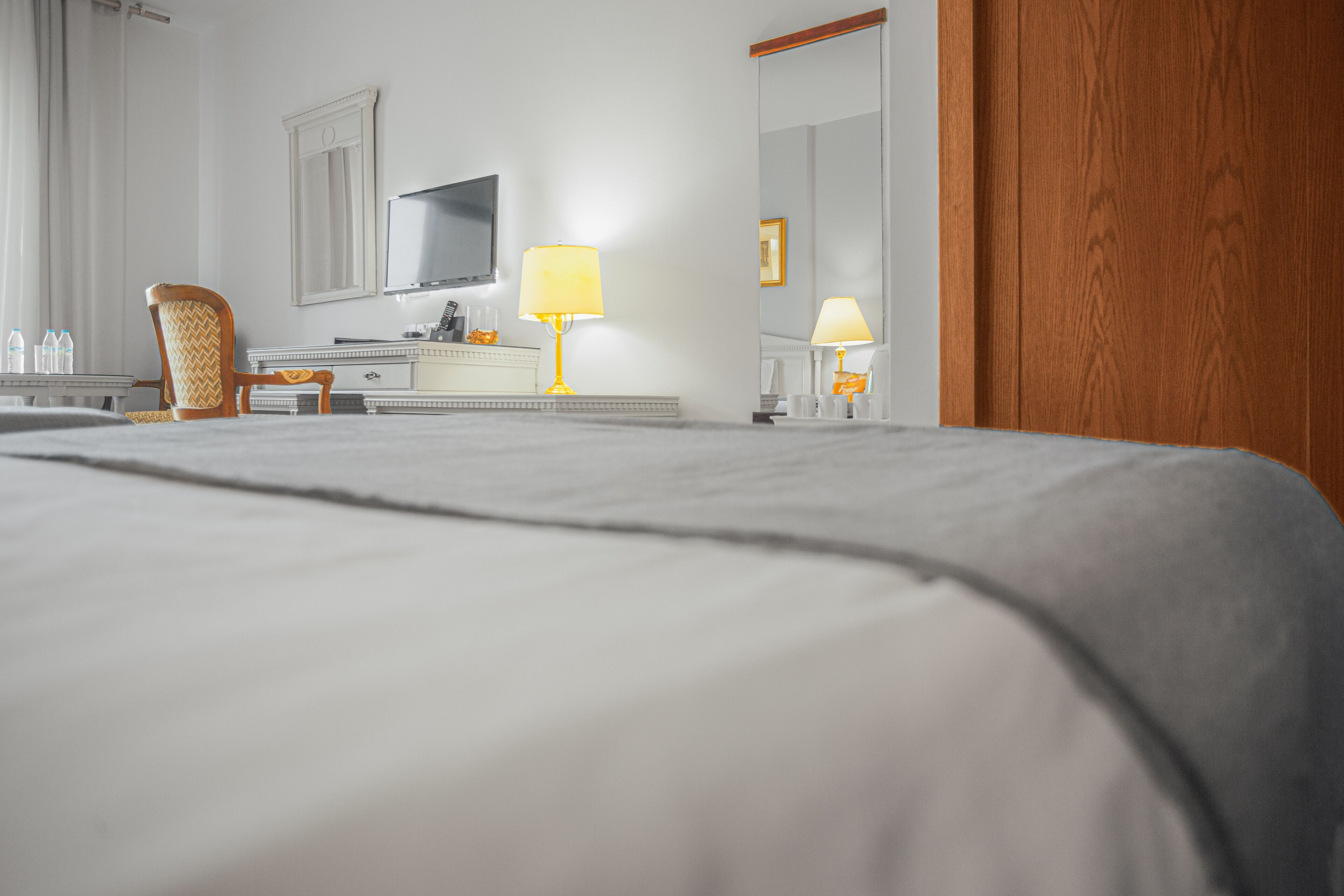 Quarto de hotel com uma cama, uma escrivaninha, uma cadeira, uma televisão e duas luminárias.