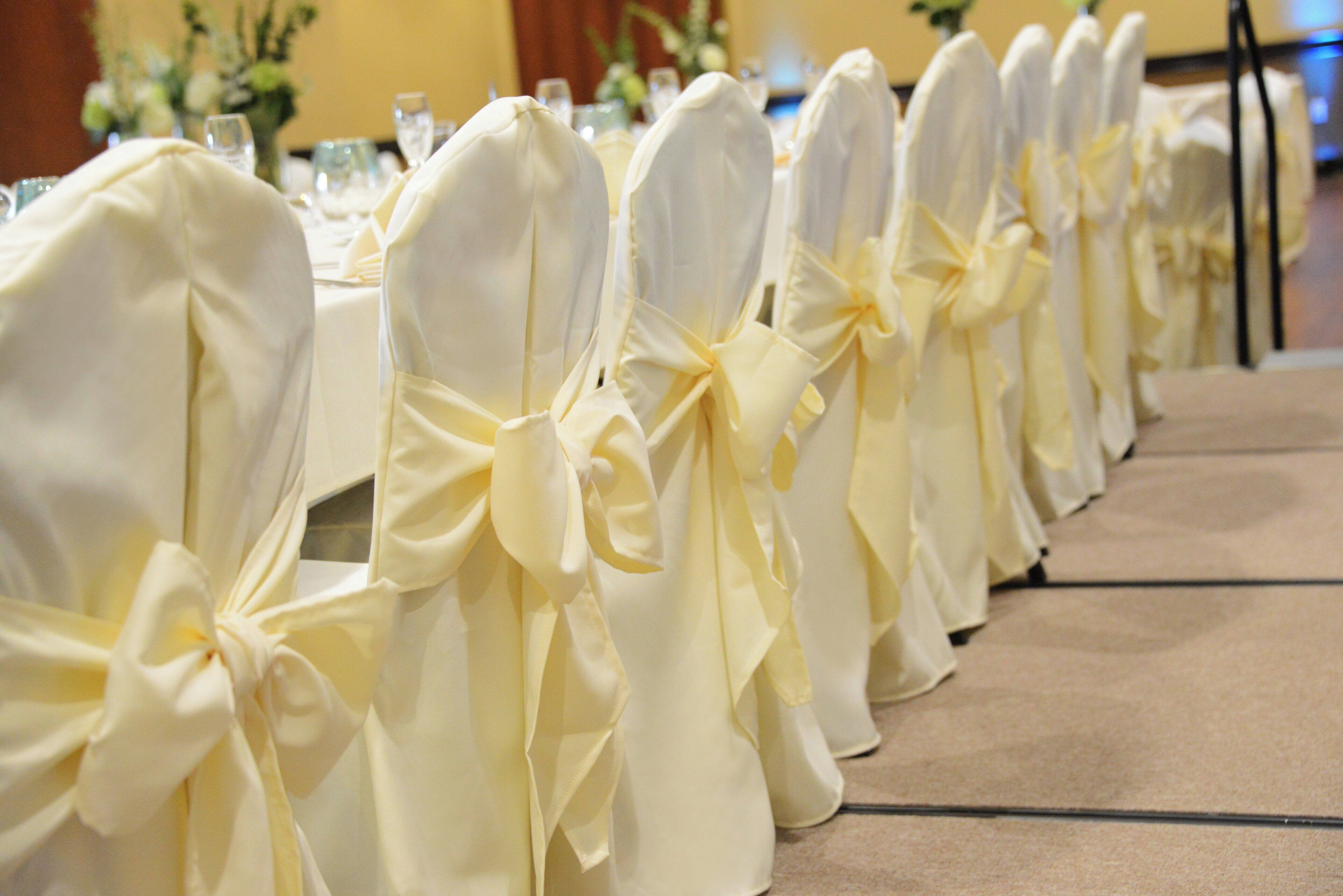 Fileiras de mesas de banquete com cadeiras cobertas por tecido branco e amarradas com fitas amarelas.