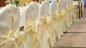 Fileiras de mesas de banquete com cadeiras cobertas por tecido branco e amarradas com fitas amarelas.