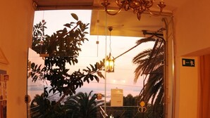 Área interna com porta de vidro que dá para o exterior, uma planta em vaso, um banco e um lustre.