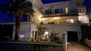 Um edifício de dois andares com varandas, uma palmeira e uma entrada bem iluminada.