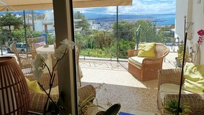 Varanda com mobiliário de vime, vista para a cidade e para o mar, e um vaso com planta.