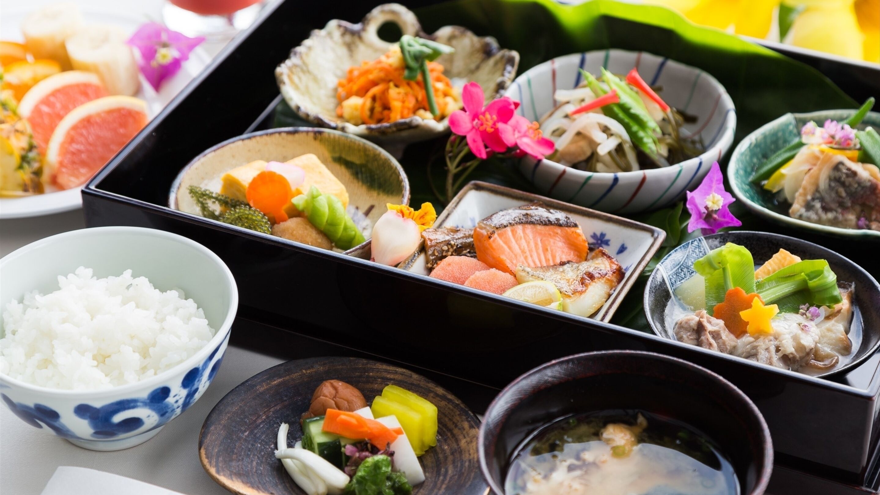 Uma tradicional bento japonesa com diversos itens de comida, incluindo arroz, peixe, legumes e uma pequena tigela de sopa.