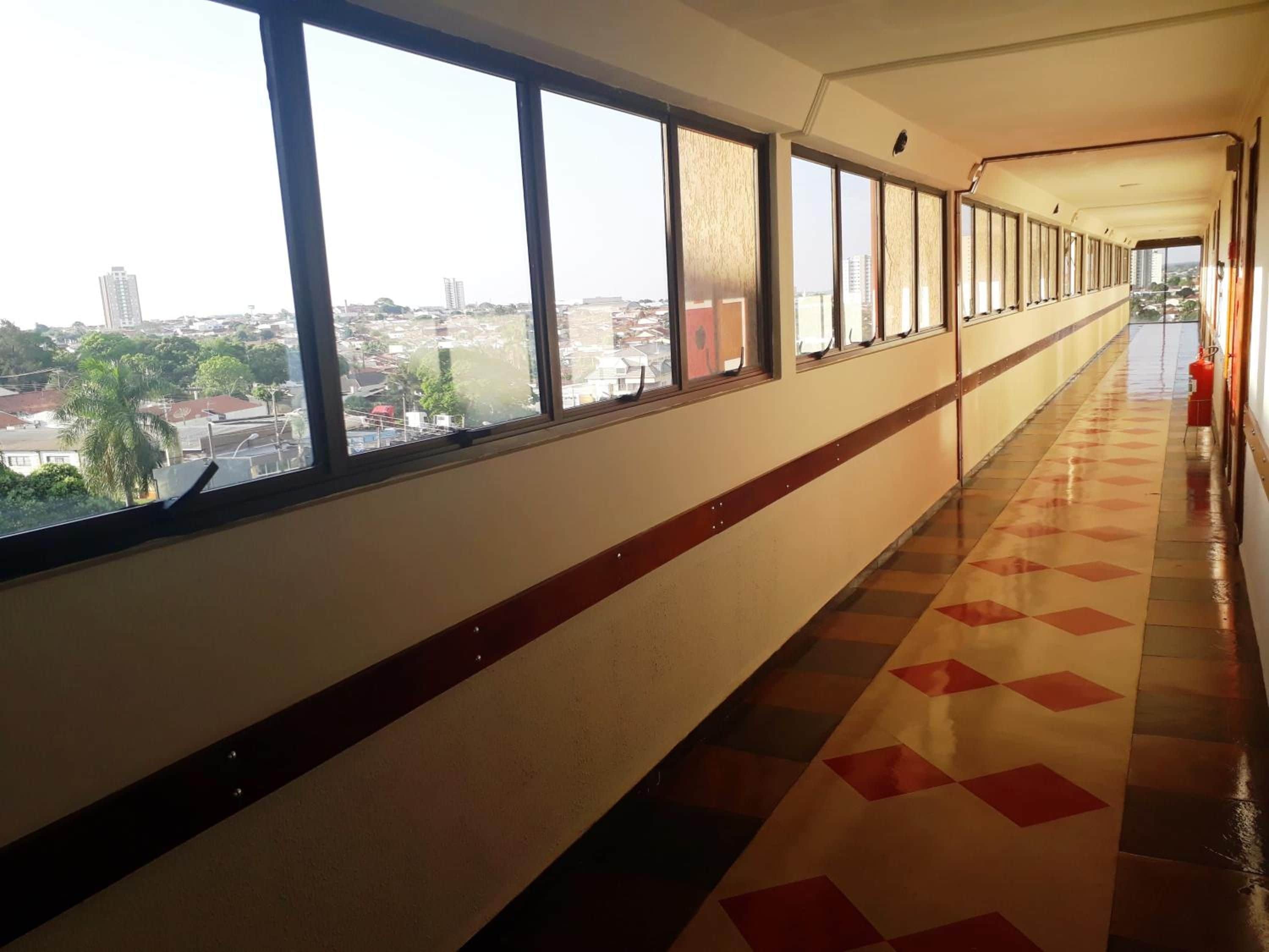 Um longo corredor com amplas janelas de um lado, piso estampado e vista para o horizonte da cidade.