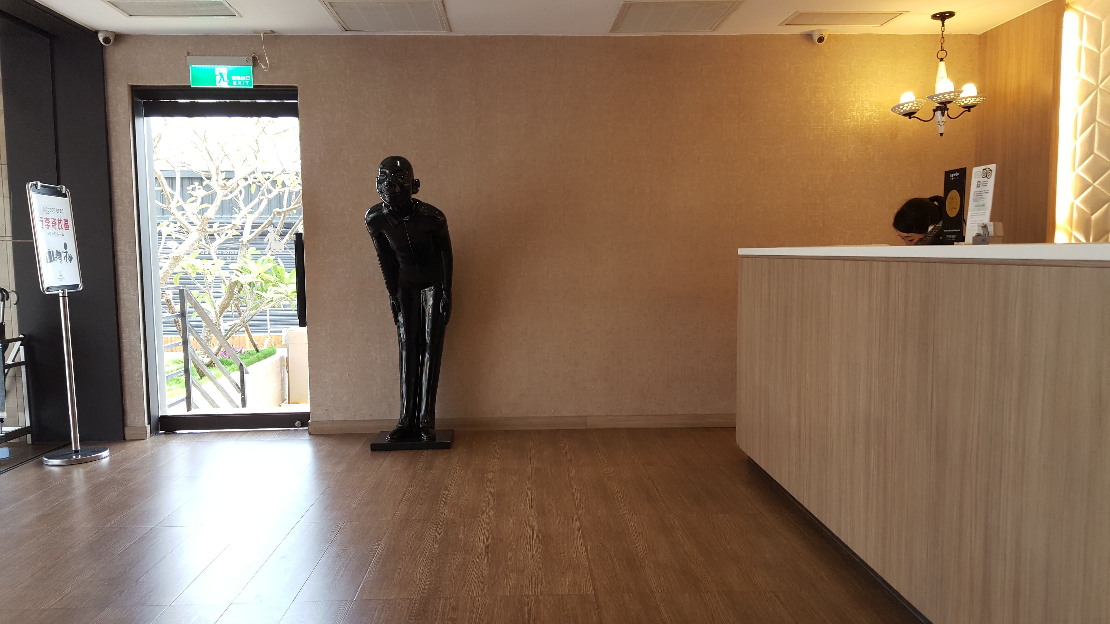 Uma área de recepção com um balcão de madeira, uma estátua preta e uma placa indicando uma saída.
