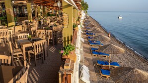 Um restaurante à beira-mar com área externa, vista para a praia e um barco na água.