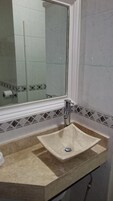 Casa de banho com lavatório quadrado, espelho e suporte para rolo de papel higiénico.