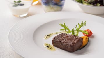 Um prato com bife, vegetais folhosos e um tomate cereja.