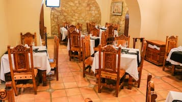 Um restaurante com cadeiras e mesas de madeira, paredes de pedra e chão de azulejos.