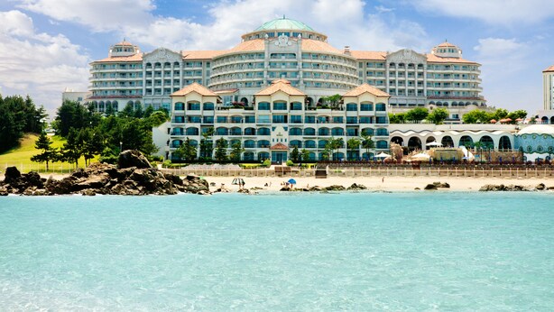 Um hotel grande com várias varandas, uma praia em primeiro plano e água azul cristalina.