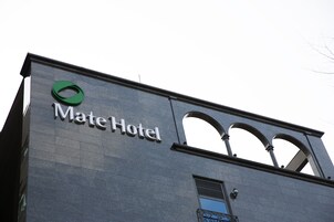 Exterior do Hotel Mate com design moderno, apresentando um logotipo marcante e o nome 'Mate Hotel' exposto na fachada.