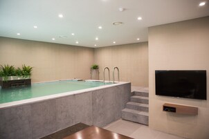 Piscina interior moderna com teto plano, colunas de som embutidas e televisão de tela plana na parede.
