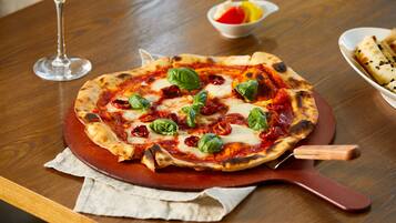 Pizza sobre uma mesa de madeira, com uma taça de vinho e uma tigela de frutas ao fundo.