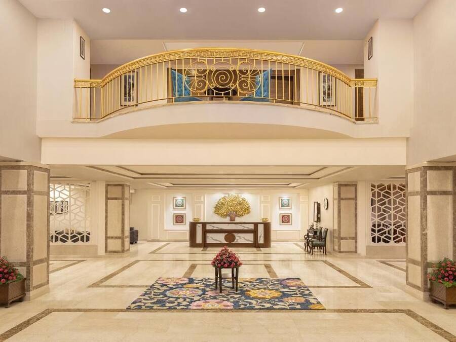 Um hall amplo com piso de mármore, uma mesa central com um vaso de flores e um corrimão de varanda curvo.