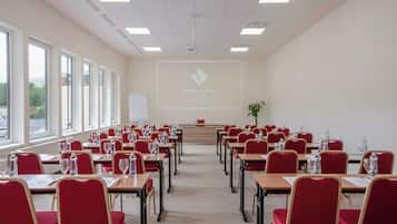 Uma sala de conferências com fileiras de mesas e cadeiras, um quadro branco e uma tela de projetor exibindo 'HOTEL SATEL POPRAD - ENTRADA'.