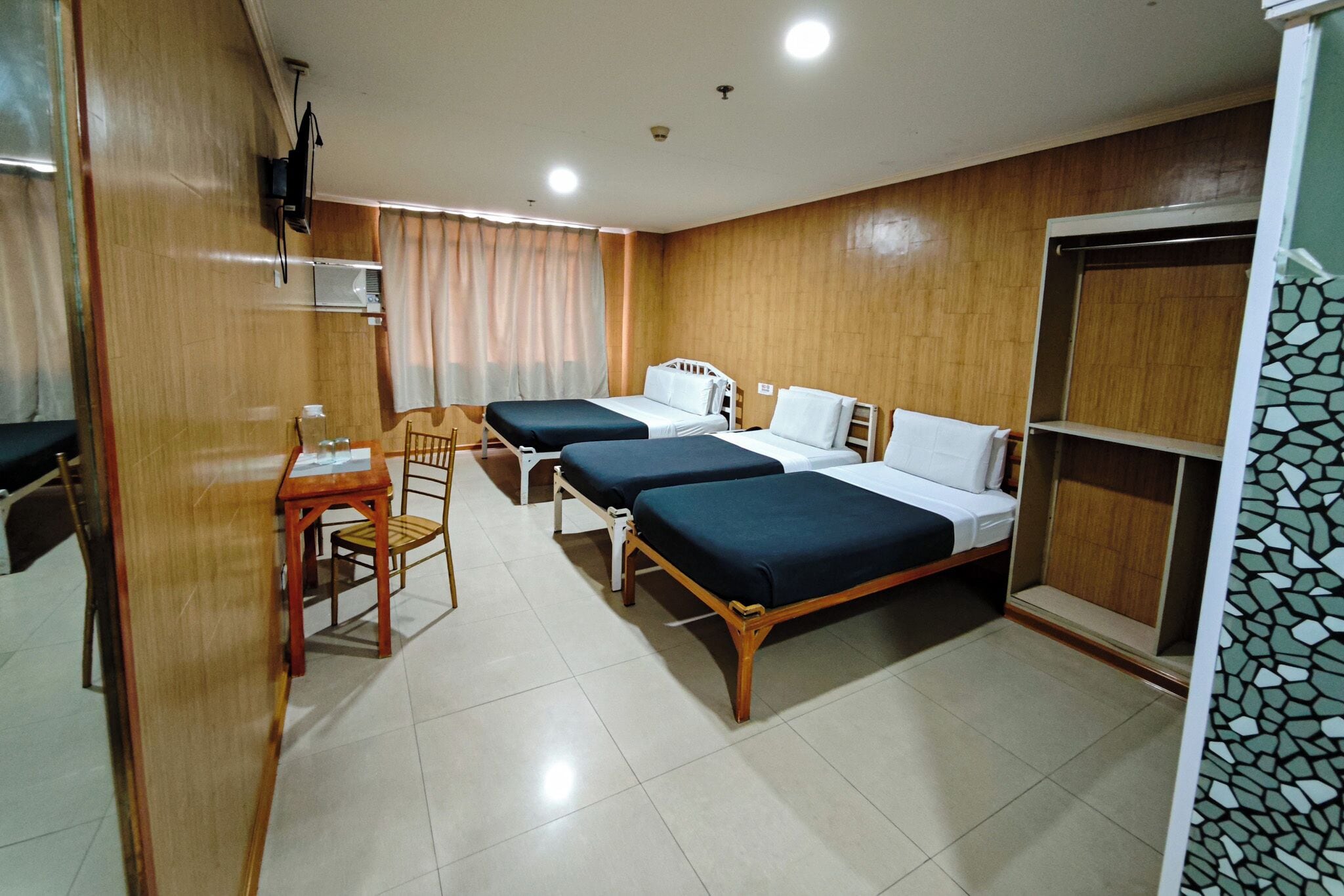 Quarto de hotel com duas camas, uma escrivaninha com cadeira, um guarda-roupa e chão em mosaico.