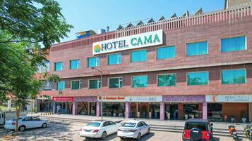 Um hotel chamado "Hotel Cama", com vários andares, fachada de tijolos vermelhos e diversas lojas no nível da rua, incluindo "Cama Banquets" e "A Boutique Hotel".