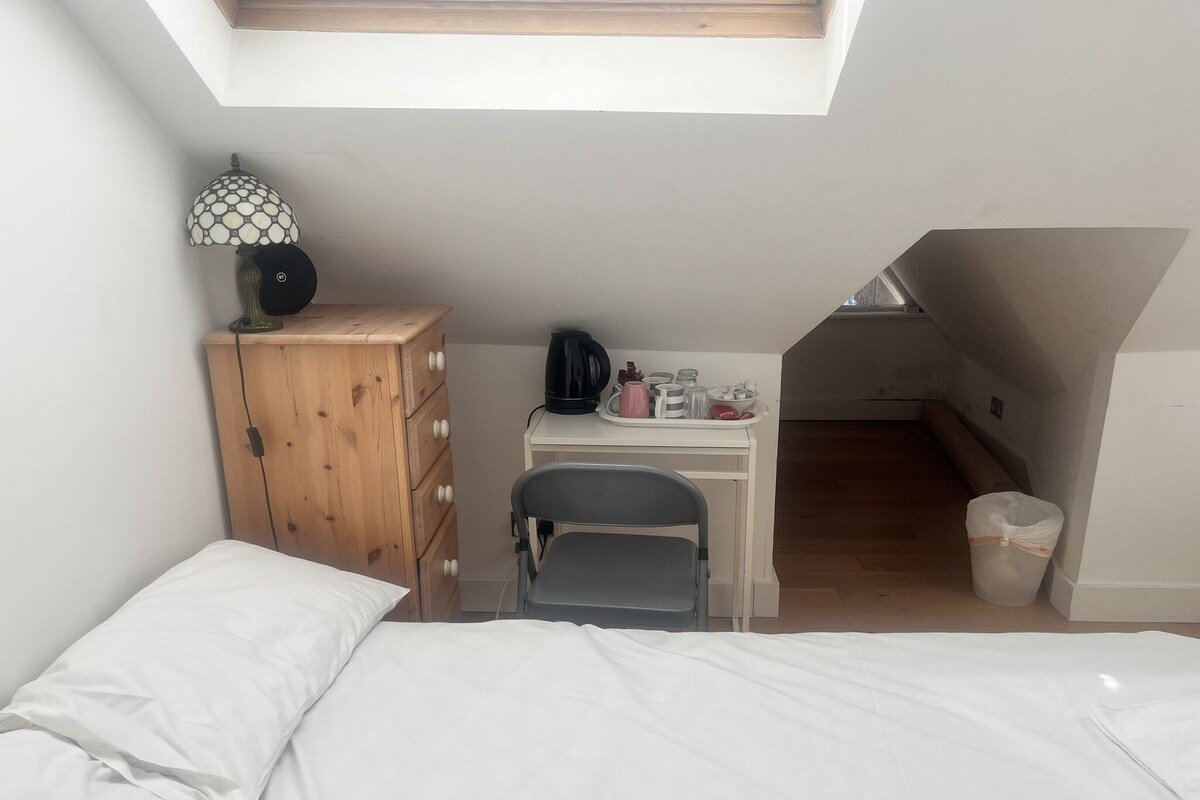 Quarto em dormitório com cama, escrivaninha, cadeira, cômoda, abajur e lixeira.