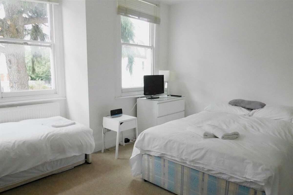 Quarto com duas camas de solteiro, uma escrivaninha com computador e uma janela.