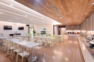 Uma sala de jantar moderna com piso de madeira, mesas e cadeiras brancas.