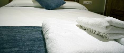 Cama bem arrumada com lençóis brancos e toalha dobrada ao lado.