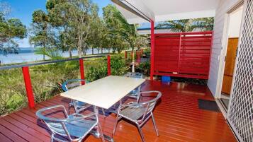 Área externa coberta com mesa e cadeiras, vista para o mar, e um portão vermelho.