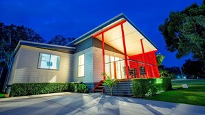 Uma casa moderna de dois andares com fachada em vidro generosa, uma parede de destaque vermelha e um gramado bem cuidado.