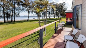 Terraço com cadeiras e mesa, com vista para uma área gramada com árvores e um corpo de água.