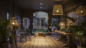 Uma sala de estar ampla com piso de madeira, um sofá verde e uma mesa de madeira. Há várias plantas em vasos e um lustre.