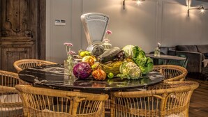 Uma sala de jantar com uma mesa redonda rodeada por cadeiras de vime, uma balança antiga e diversos vegetais.