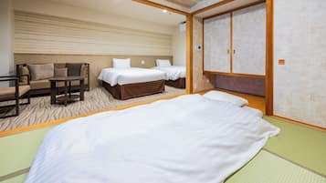 Quarto de hotel com duas camas, um sofá, uma mesa pequena e uma porta tradicional japonesa deslizante.