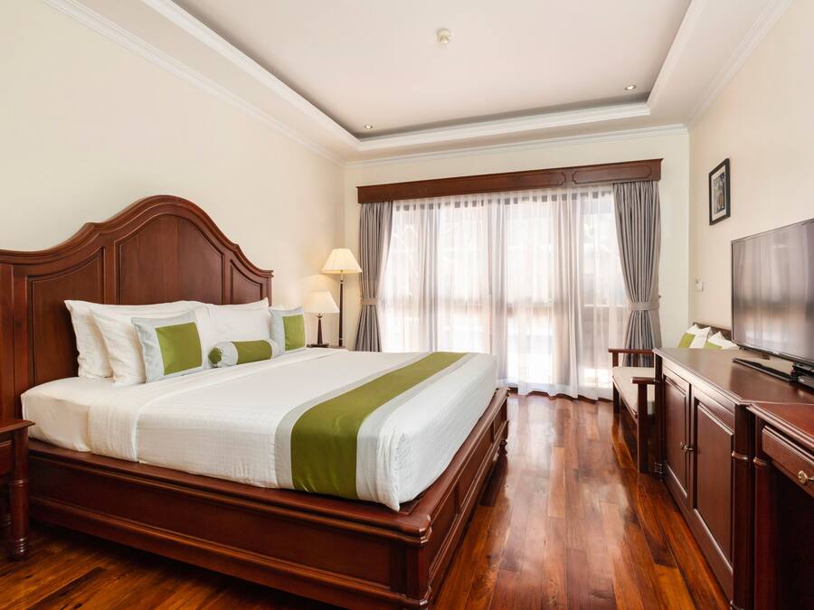 Um quarto espaçoso com uma cama grande, cabeceira de madeira e uma televisão sobre um móvel de madeira.