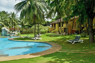 Uma área de piscina com espreguiçadeiras, palmeiras e um edifício com varandas.