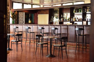 Uma área de bar com diversas opções de assento, incluindo banquetas e mesas, uma variedade de garrafas nas prateleiras e um design de parede estampado.