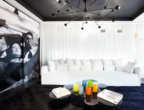 Uma sala de estar moderna com um sofá branco, um lustre preto e uma mesa de centro com livros e copos coloridos.