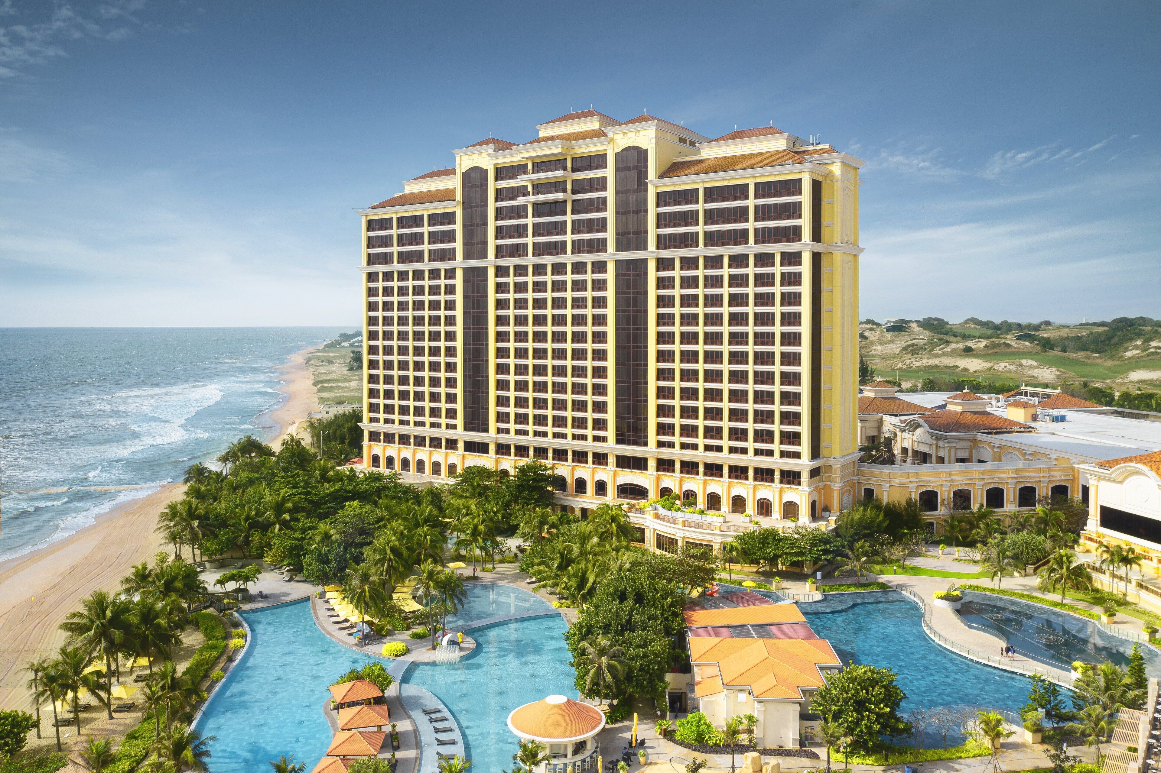Um hotel com ampla área de piscina, vista para a praia e vários edifícios.