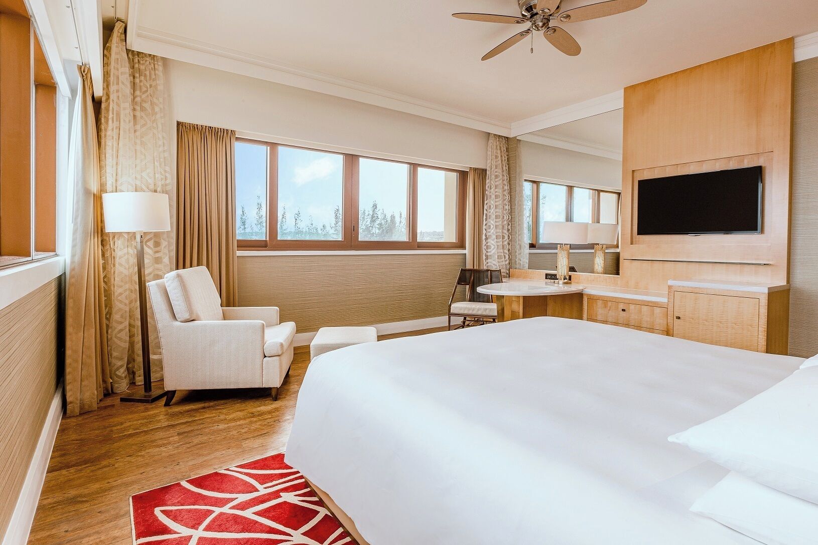 Quarto de hotel com cama grande, escrivaninha, cadeira, televisão e janela com cortinas.