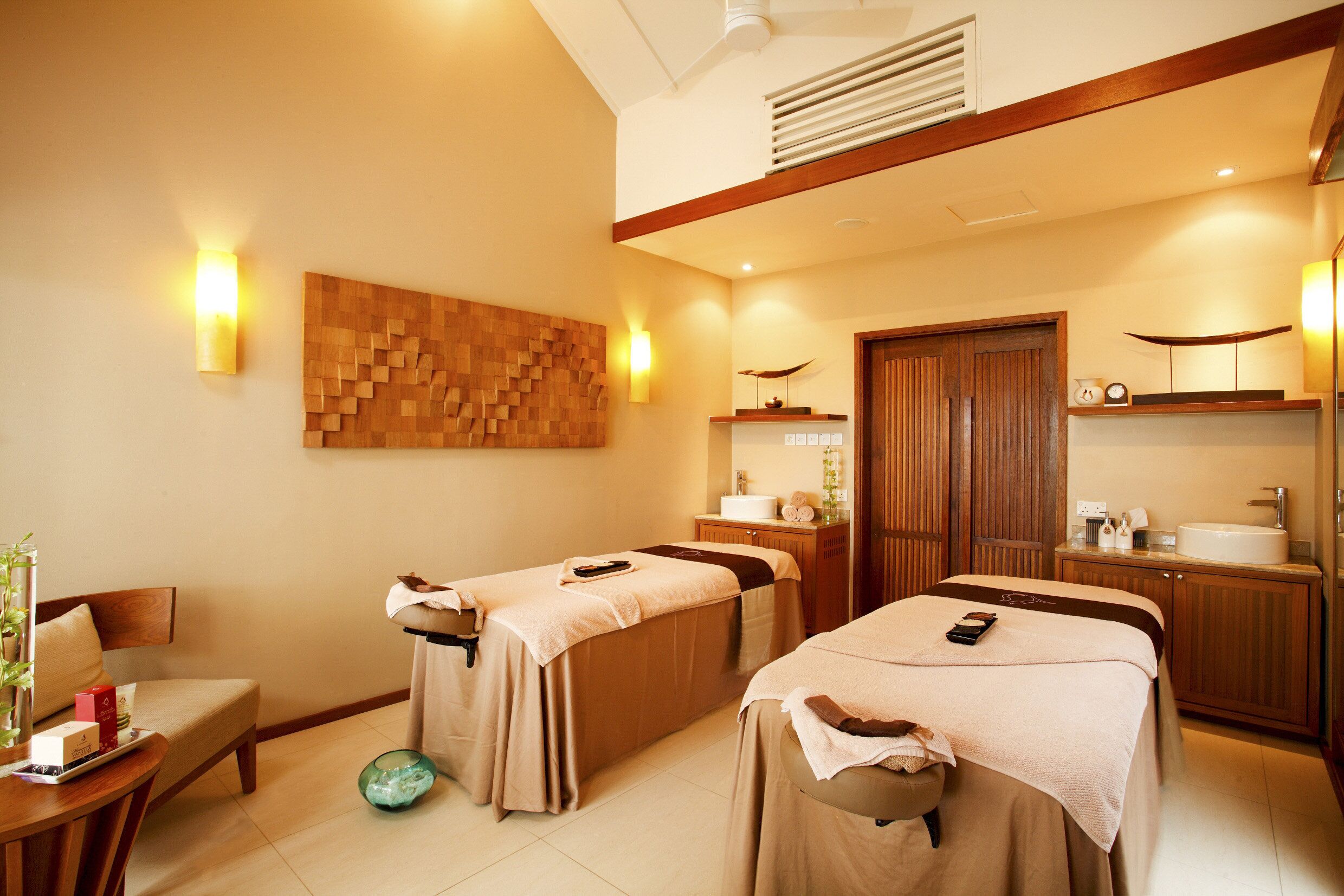 Uma sala de spa com duas mesas de massagem, um armário de madeira, uma pia e um aplique na parede.