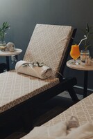 Quarto com cama, uma cadeira e uma pequena mesa com bebida e planta.