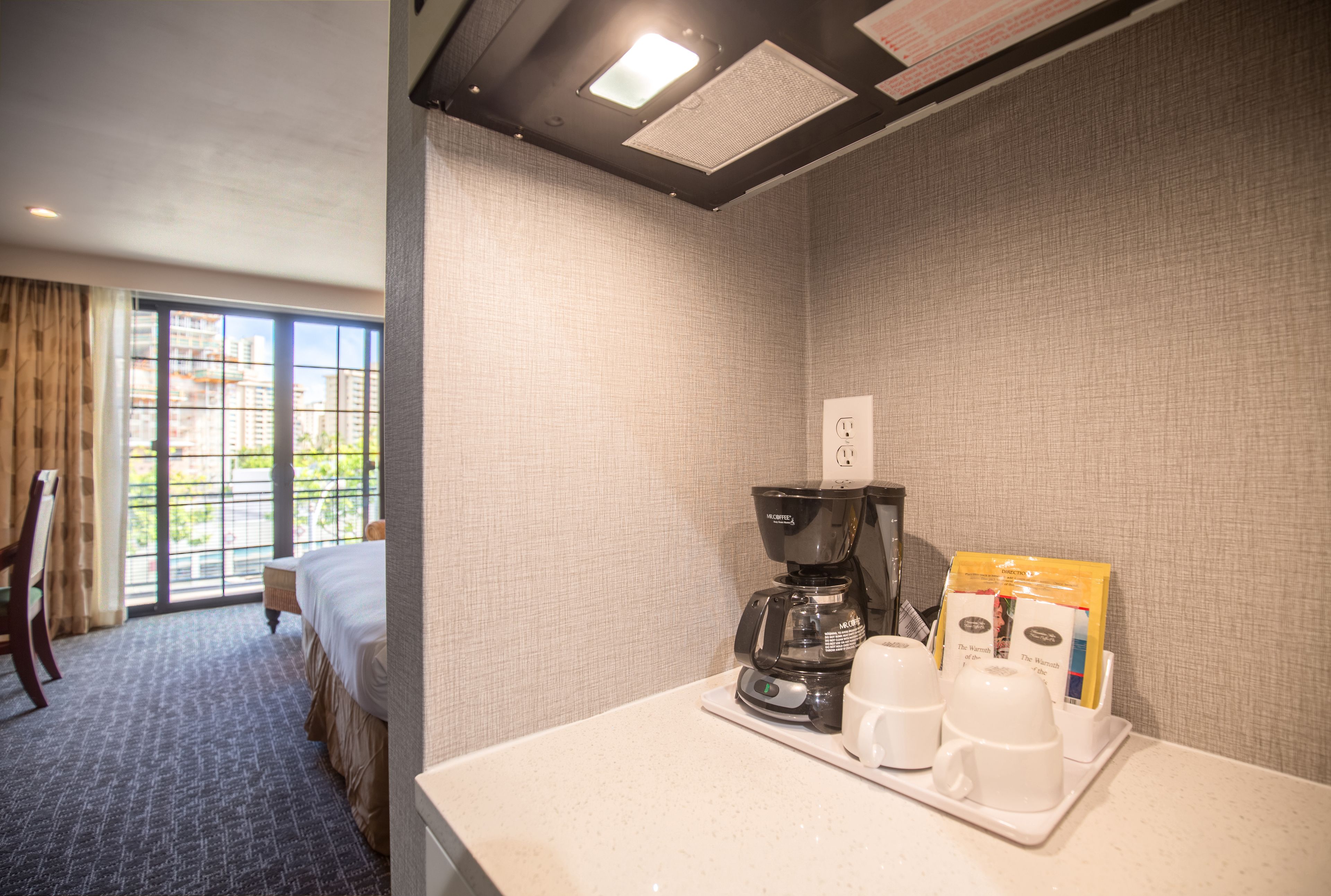 Quarto de hotel com cama, cafeteira, xícaras e bandeja com cardápio.