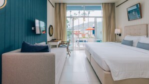 Quarto de hotel com cama, sofá, televisão, escrivaninha e vista para a piscina e palmeiras.