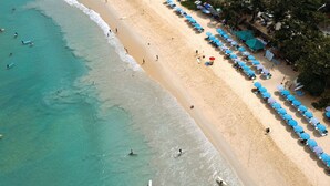 Vista aérea de uma praia com águas turquesa cristalinas, areia dourada e fileiras de guarda-sóis azuis.