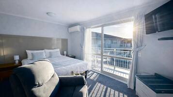 Quarto de hotel com cama, poltrona, escrivaninha, televisão e varanda com vista para a cidade.