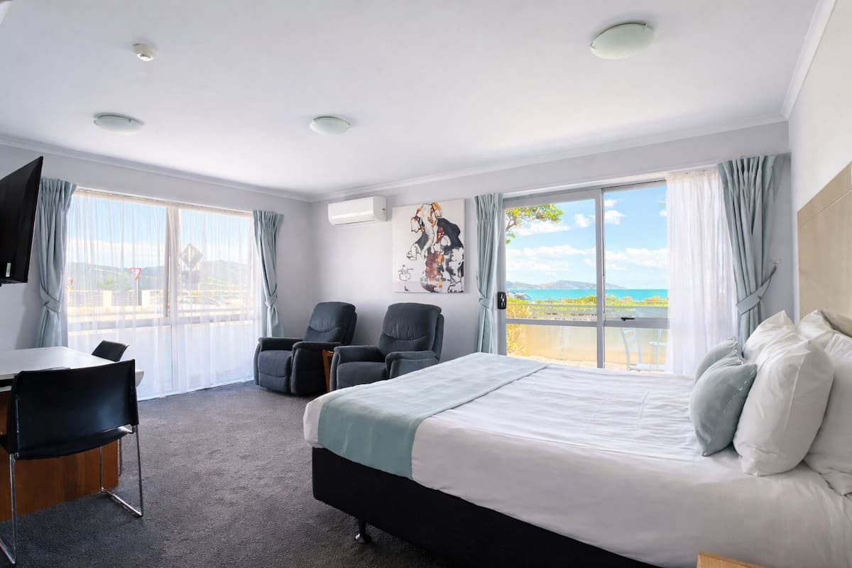 Quarto de hotel com uma cama grande, duas poltronas, uma escrivaninha e uma televisão.