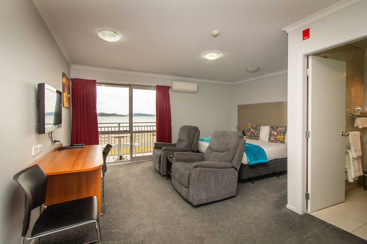 Quarto de hotel com varanda, uma escrivaninha com cadeira, sofá e cama.