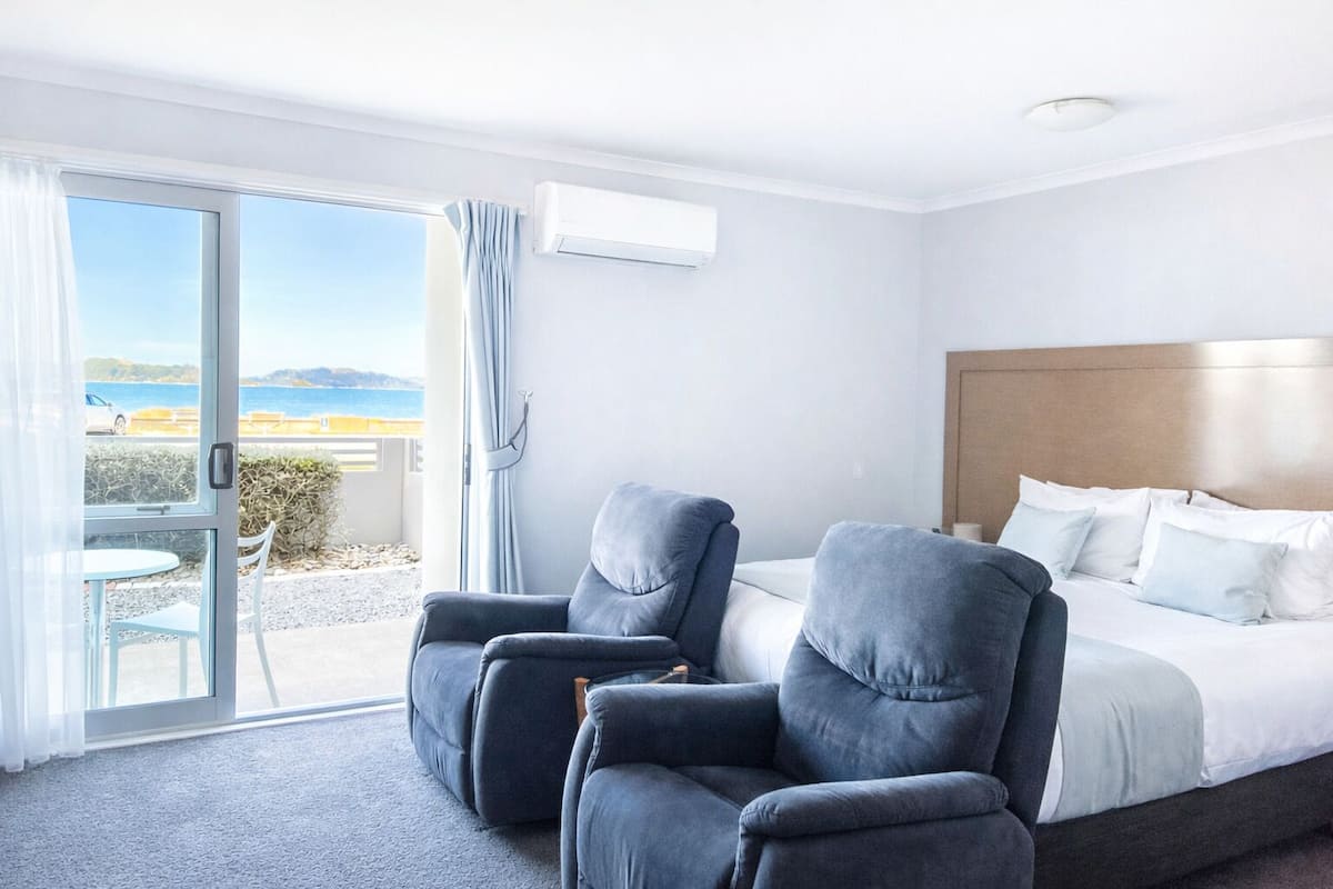 Quarto de hotel com cama, duas poltronas, vista para o mar e ar condicionado.