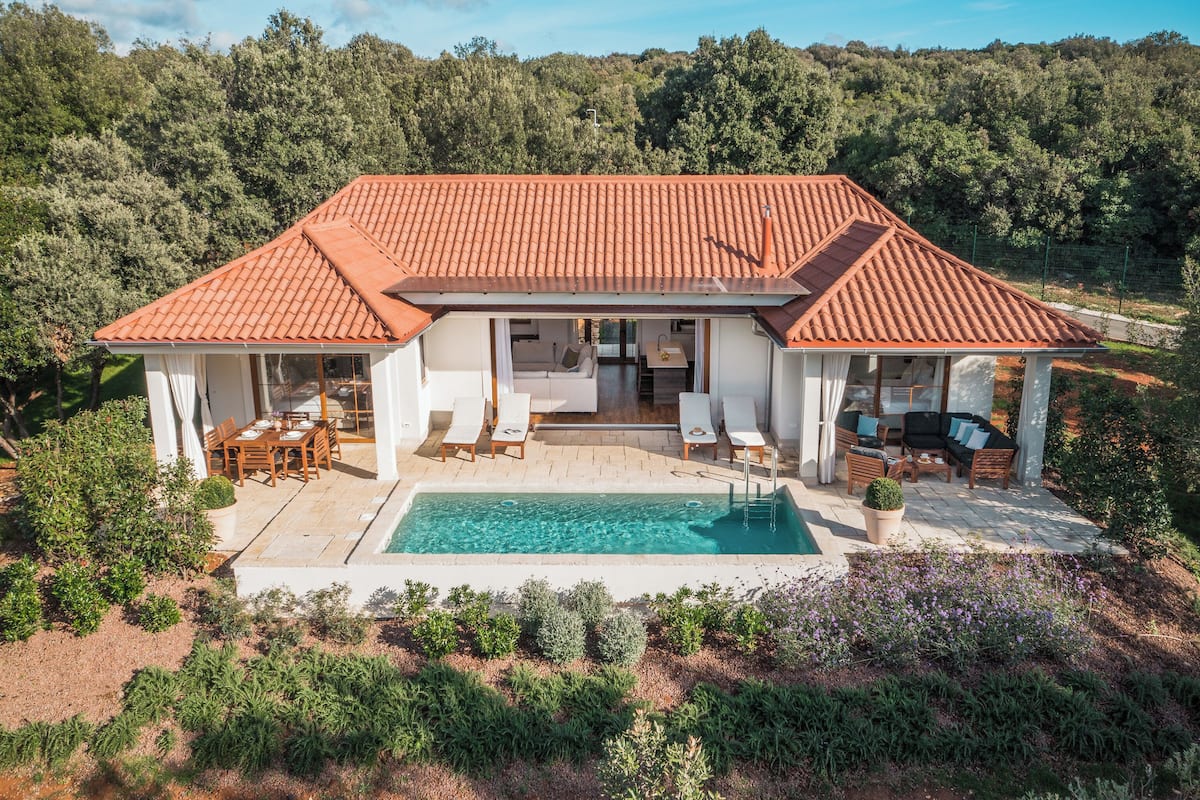 Uma casa com piscina, área de estar externa e vista para a floresta ao redor.