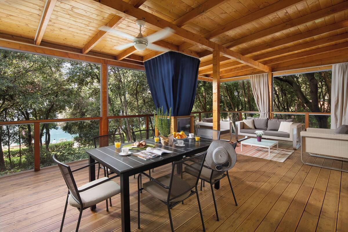 Área externa coberta com mesa posta para café da manhã, um sofá e vista para o exterior.